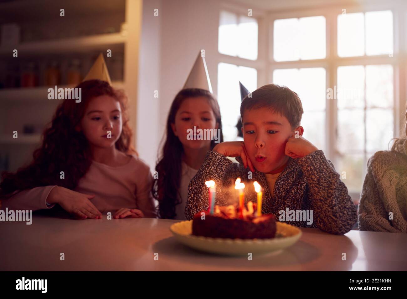 Boy Blowing Out Candles On Cake As He Celebrates Birthday With Group Of ...