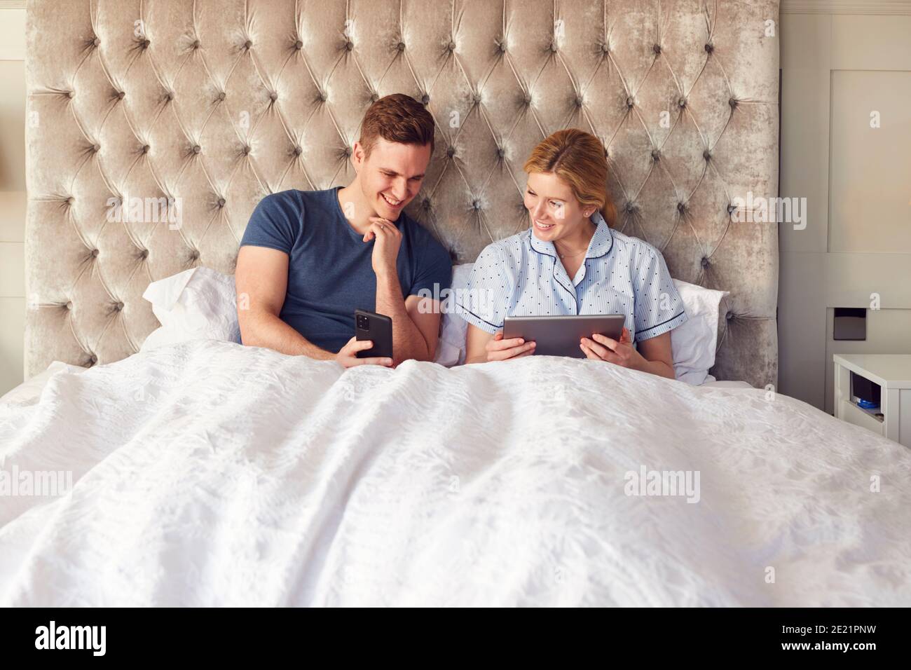 Couple At Home In Bed Self Isolating Using Digital Tablet And Mobile ...