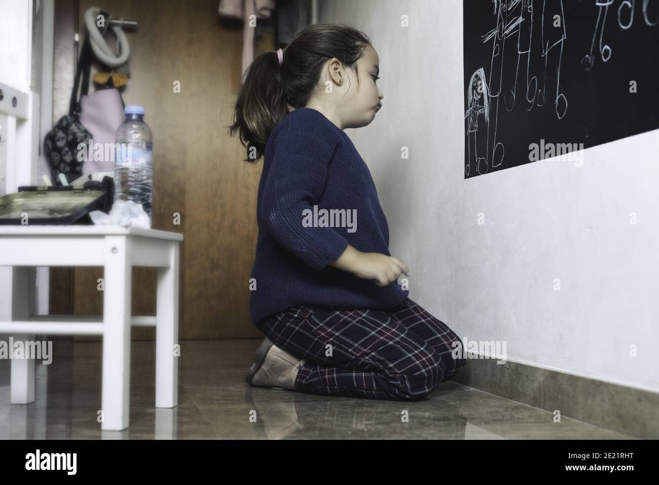 Caucasian little girl sitting on the ground drawing on the blackboard ...