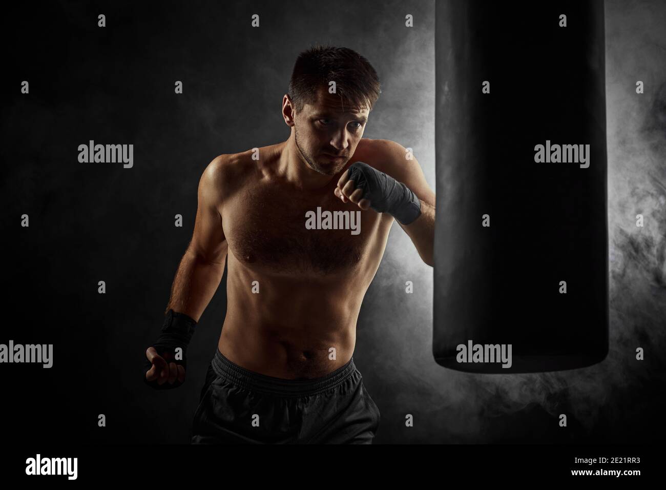 Aggressive boxer training defense and attacks in boxing bag on black ...