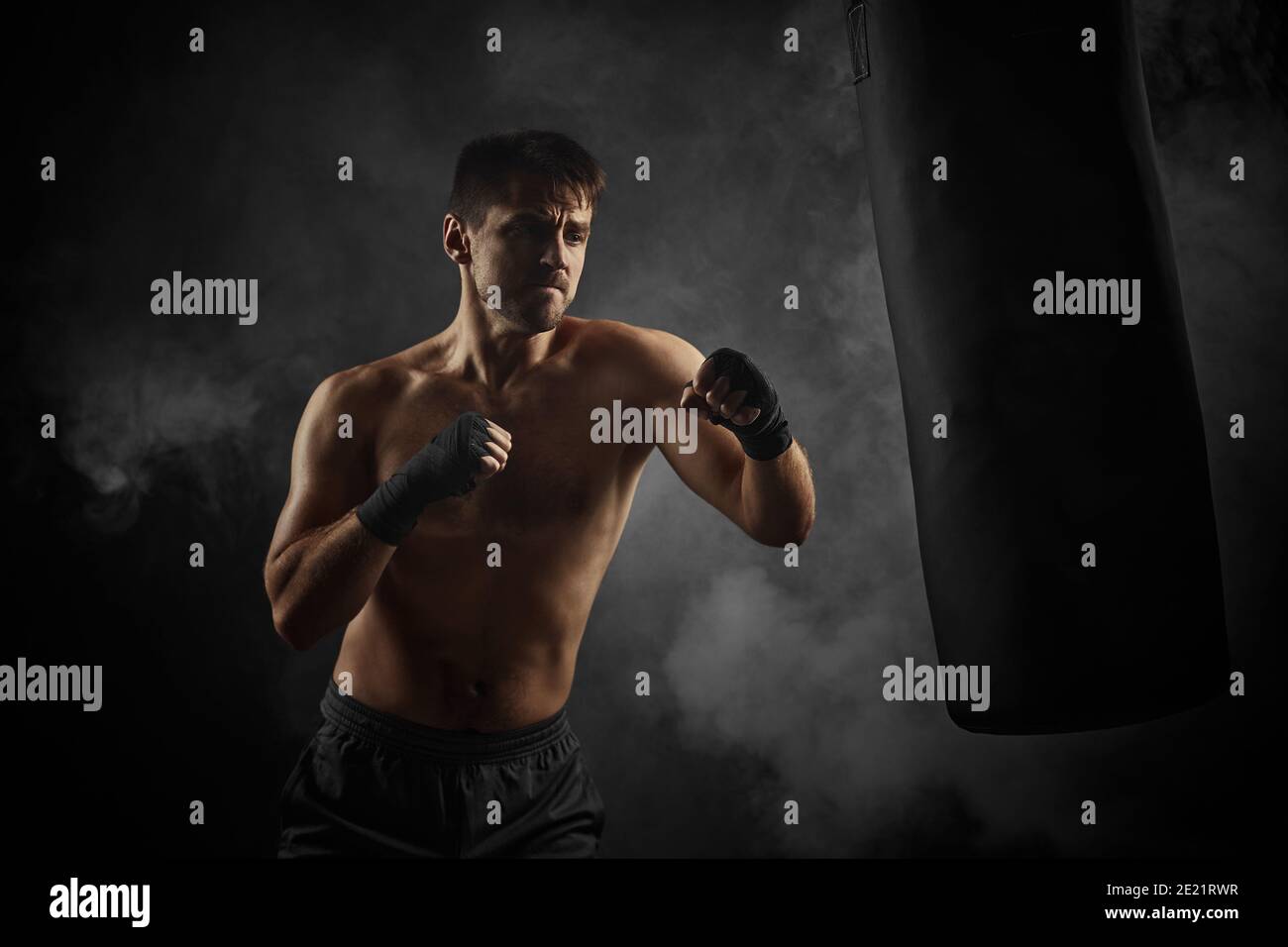 sporty shirtless boxer in black boxing wraps punching in boxing bag on ...