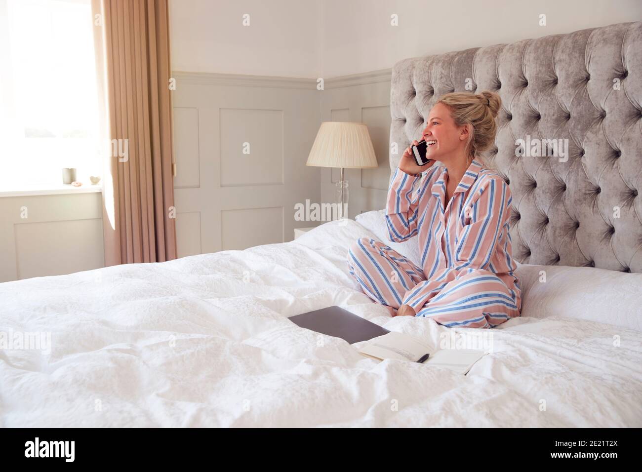 Businesswoman In Pyjamas Sitting On Bed Making Call On Mobile Phone ...