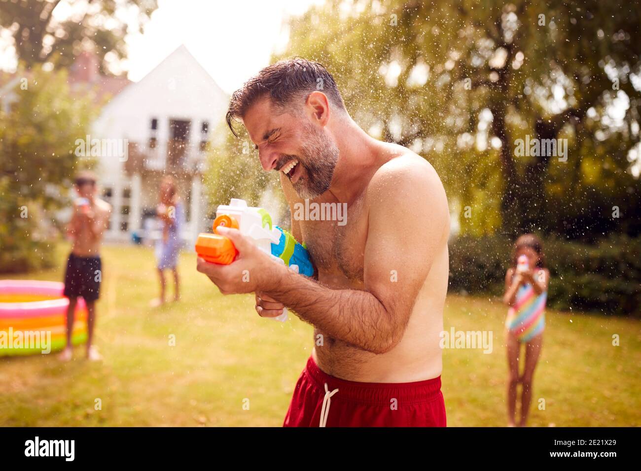 Family Wearing Swimming Costumes Having Water Fight With Water Pistols ...