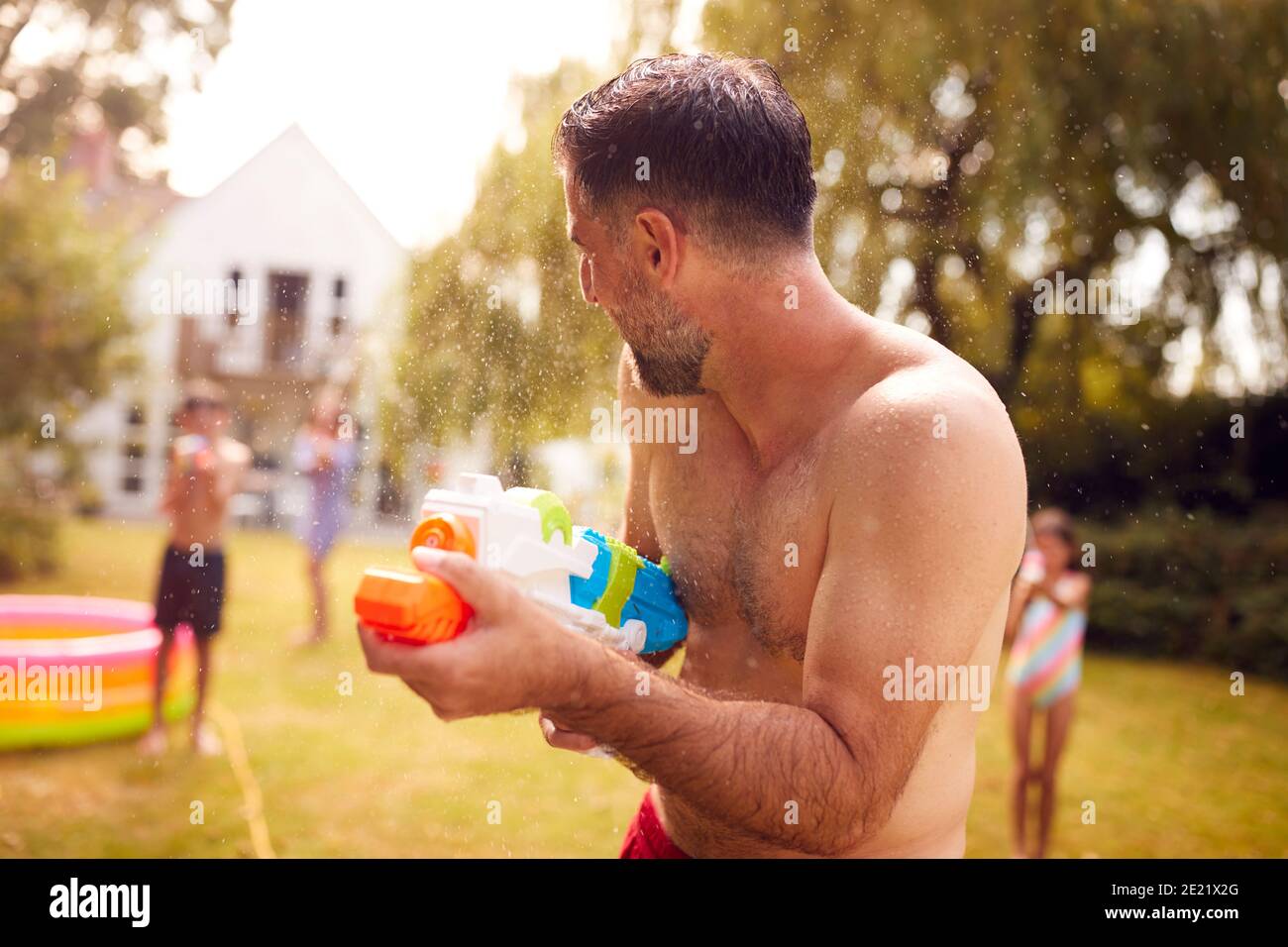 Family Wearing Swimming Costumes Having Water Fight With Water Pistols ...
