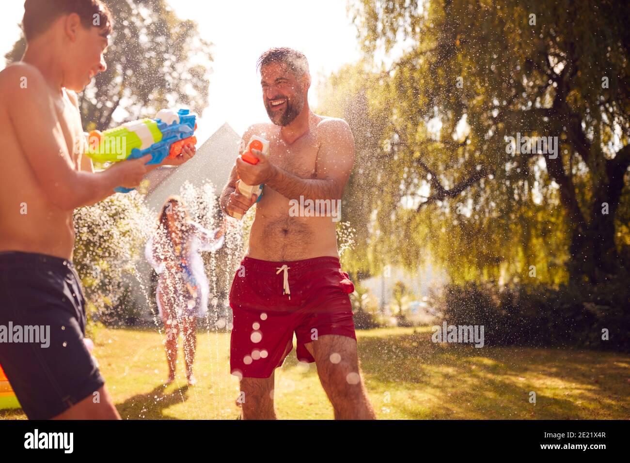 Family Wearing Swimming Costumes Having Water Fight With Water Pistols ...