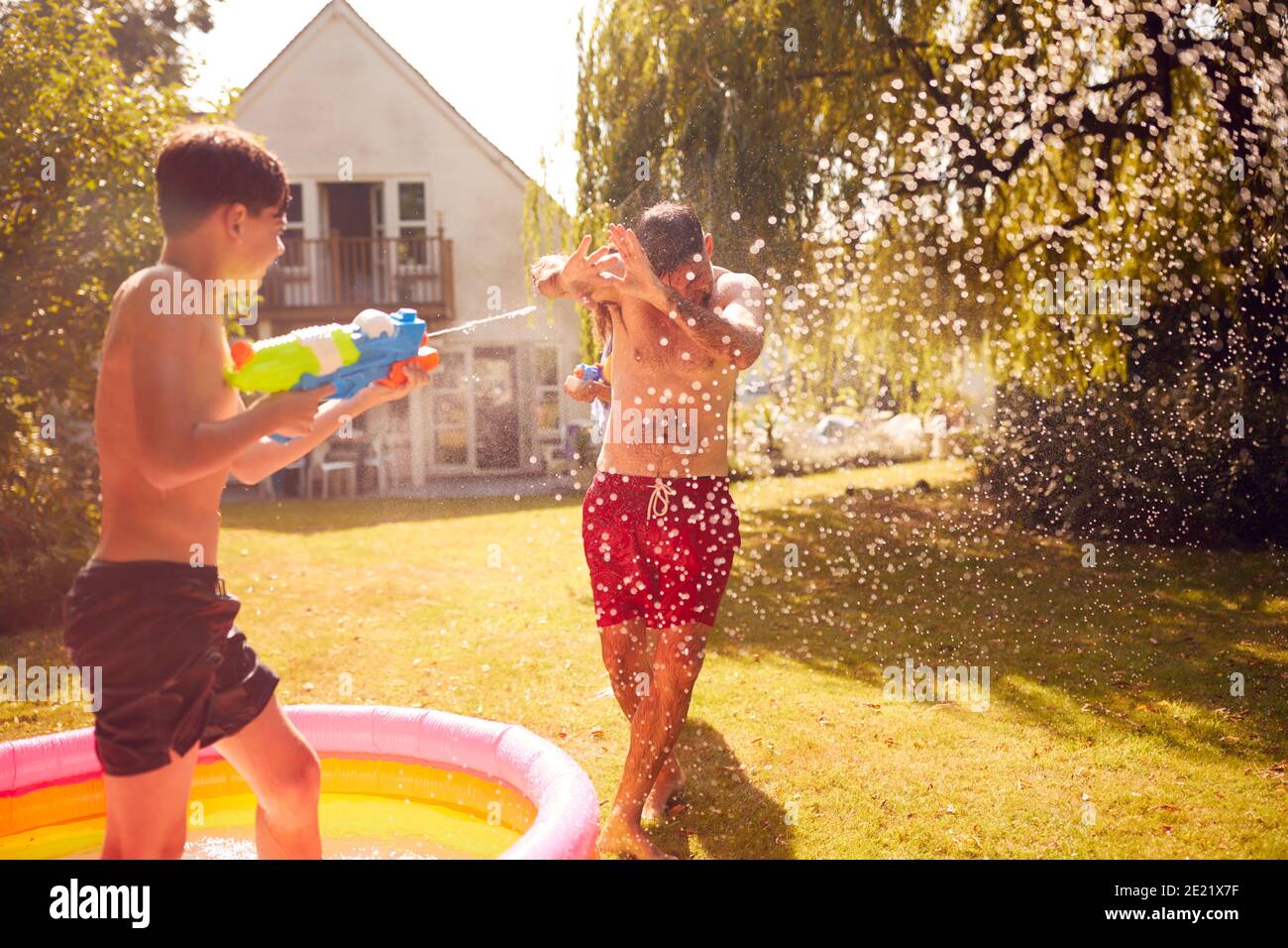 Family Wearing Swimming Costumes Having Water Fight With Water Pistols ...