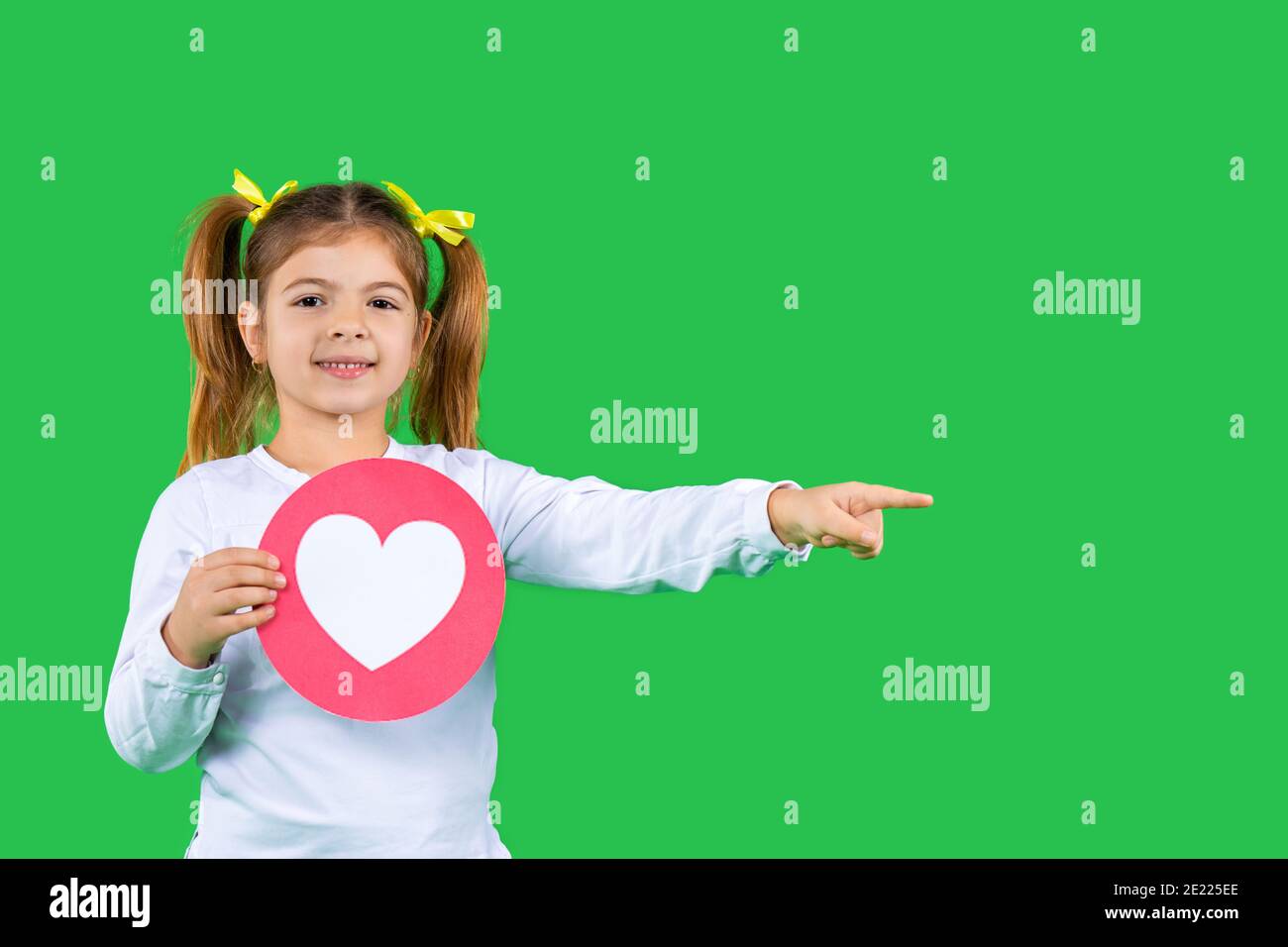 A child on a green background with a heart shows his index finger to ...