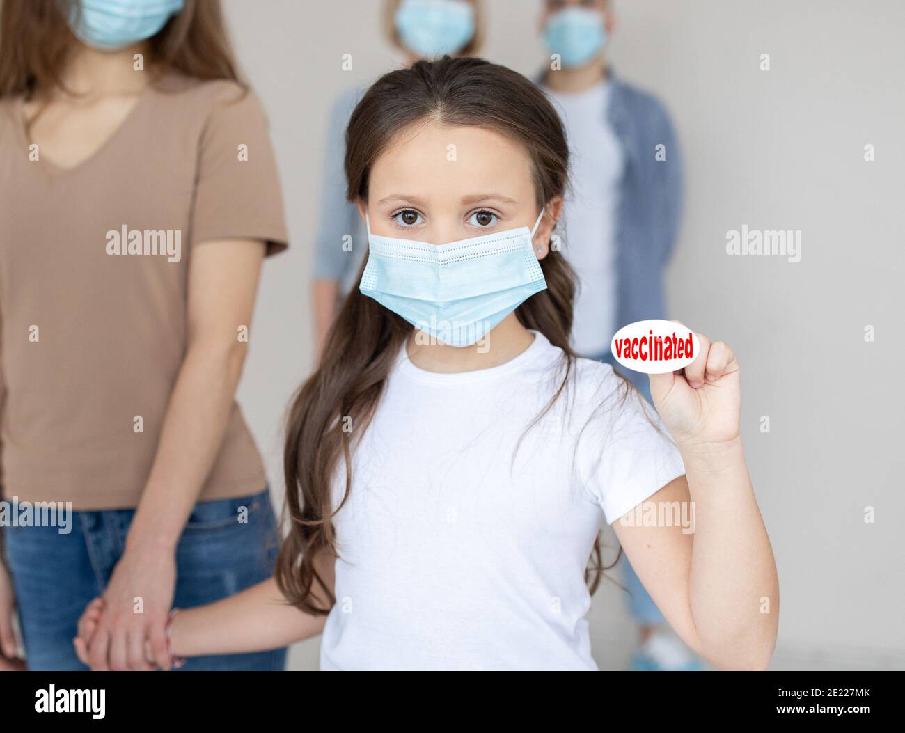 Cute girl in face mask holding her mom's hand, showing VACCINATED badge ...