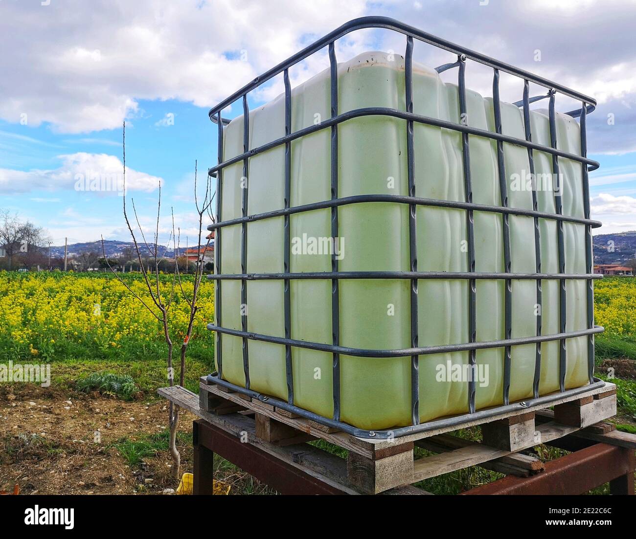 Plastic water tank in a farm field under a blue cloudy sky and sunlight ...