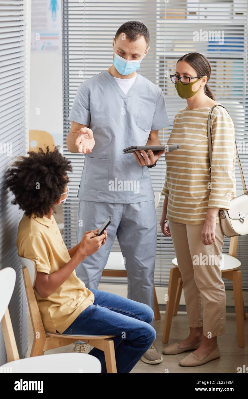 Vertical full length portrait of young male doctor talking to patients ...