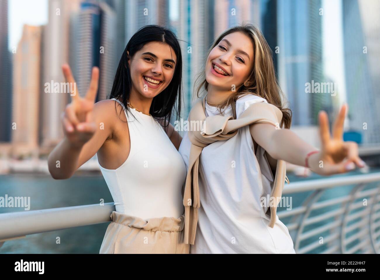 Portrait of two smiling young girls waving to camera while standing ...