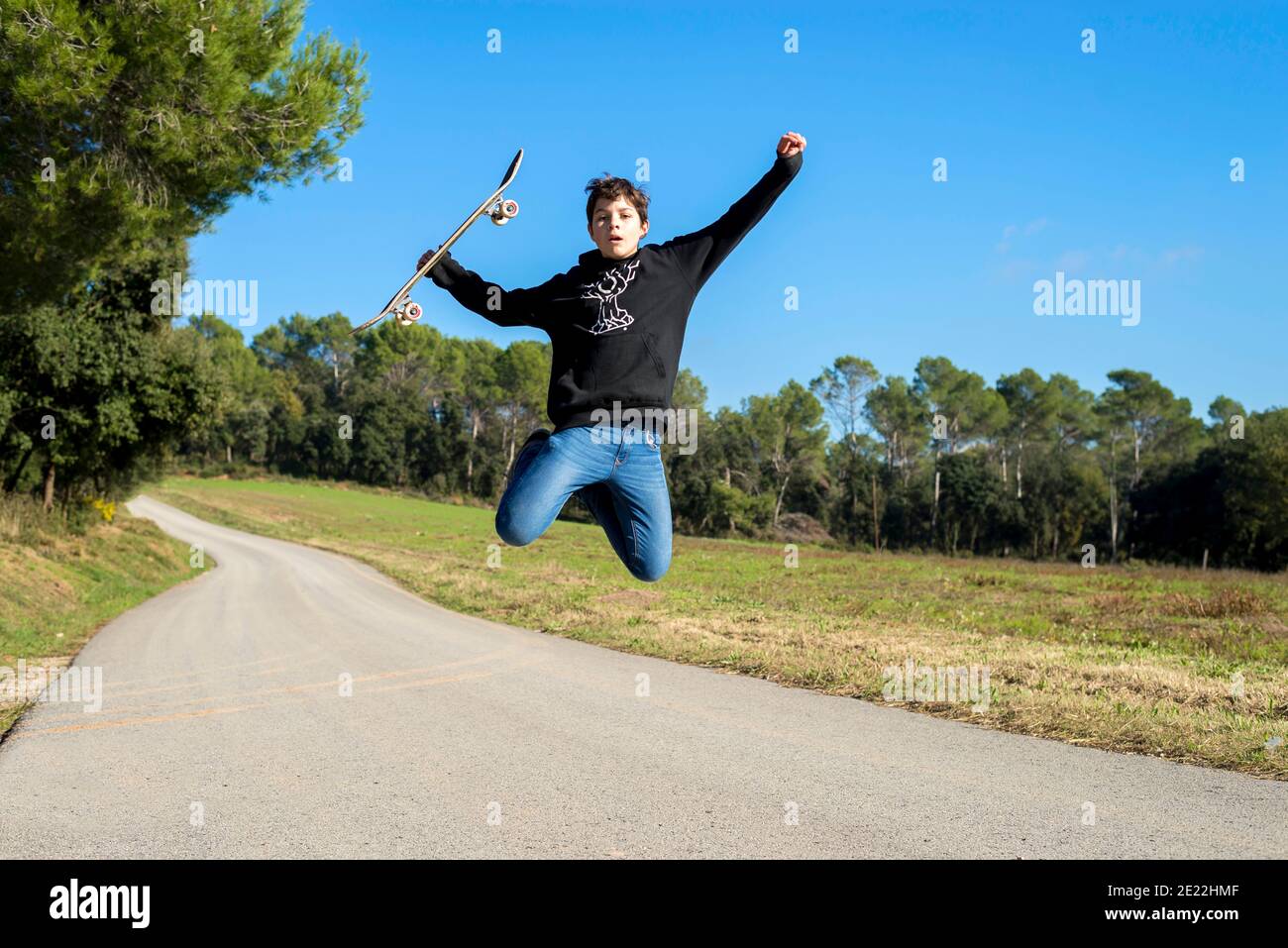 Action shot of a young skater teen male jumping high on a hill road ...