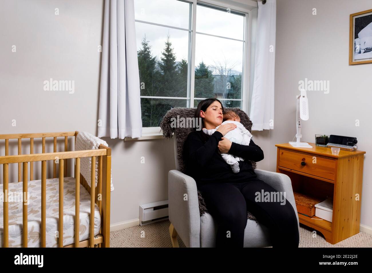 A mother holds her baby over her shoulder and rocks in a rocking chair ...