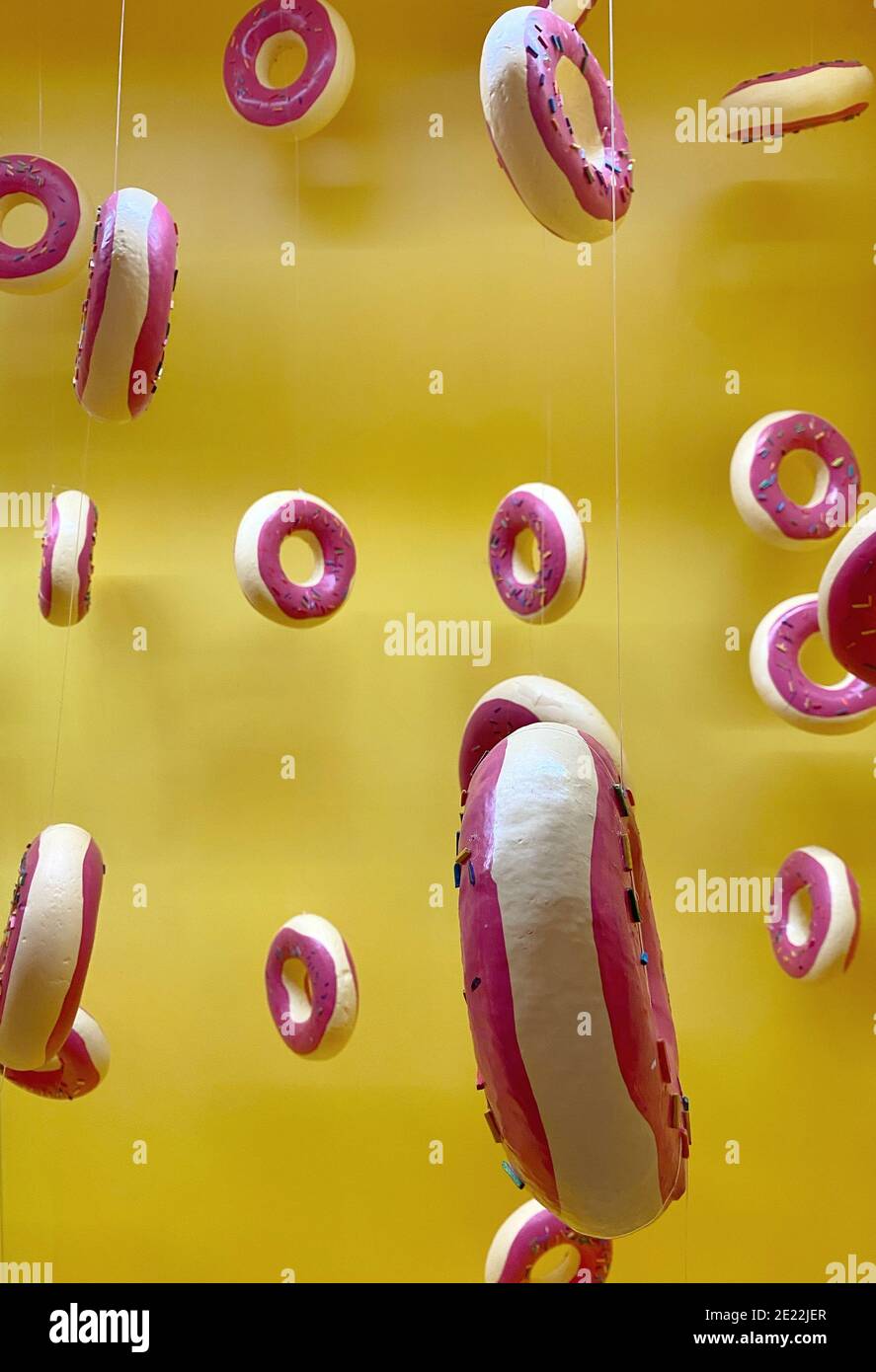 Vertical shot of donut figures hanging from ropes against a yellow ...