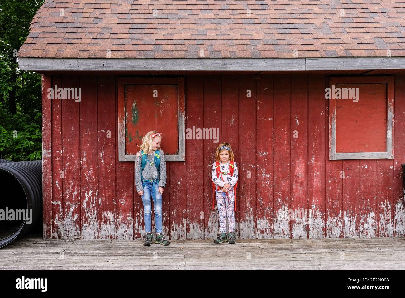 two girls standing together against weathered red barn wall Stock Photo ...