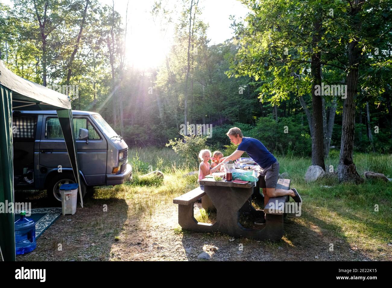 family sitting together at dinner while camping in woods in summertime ...