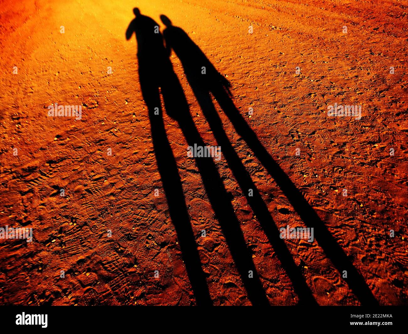 Shadow of two people holding hands walking down a dirt road together ...