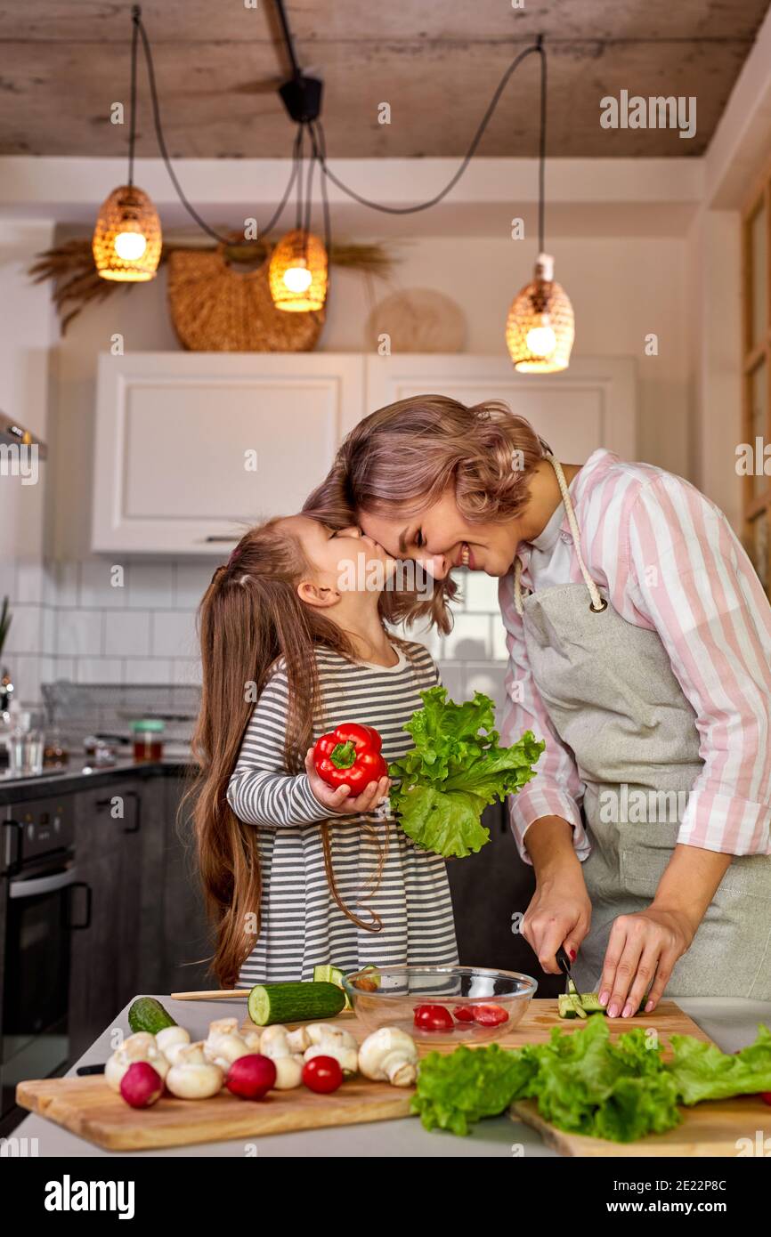 lovely mother and daughter kissing in the kitchen while cooking ...