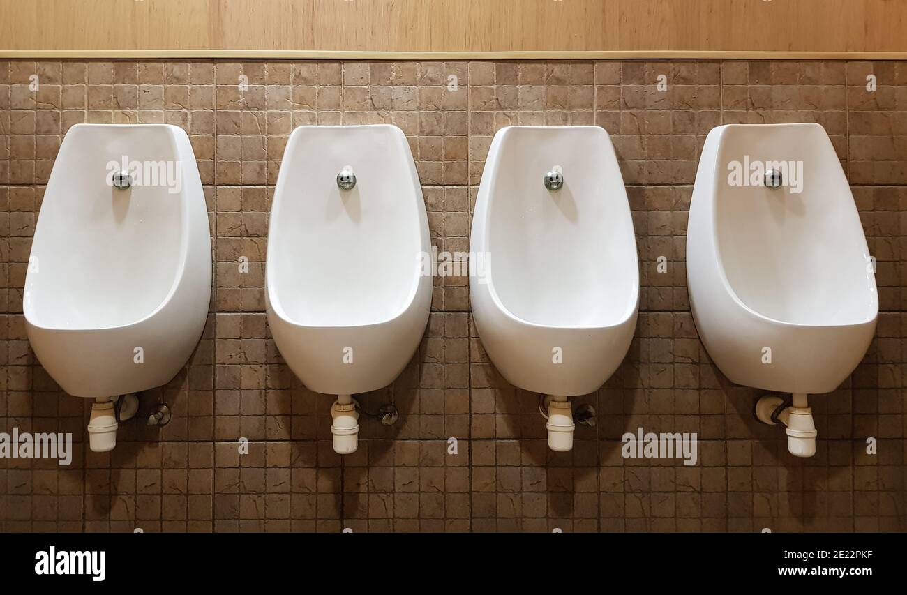 Four urinals lined up on the tiled wall of a modern men's public toilet ...