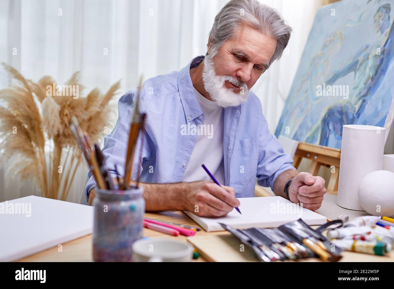 painter is drawing at home in light room, gray bearded man is creating ...