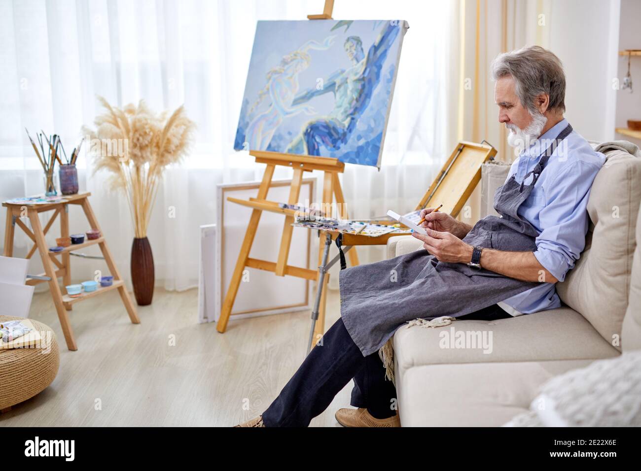 painter man sitting on sofa, concentrated on work with pencil, sit ...