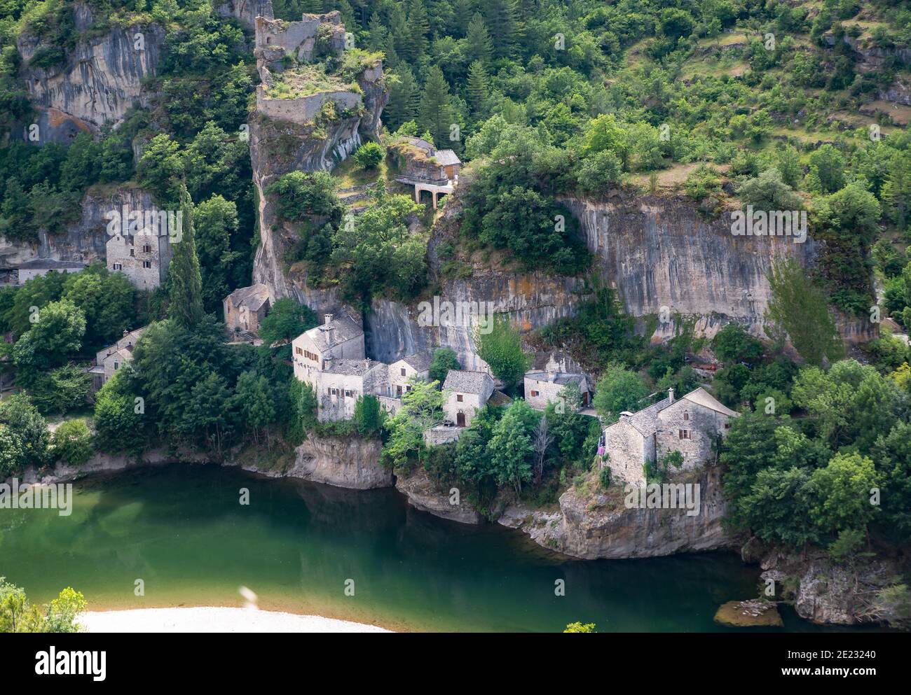 Aerial view of stone buildings built on a cliff next to a green shaded ...