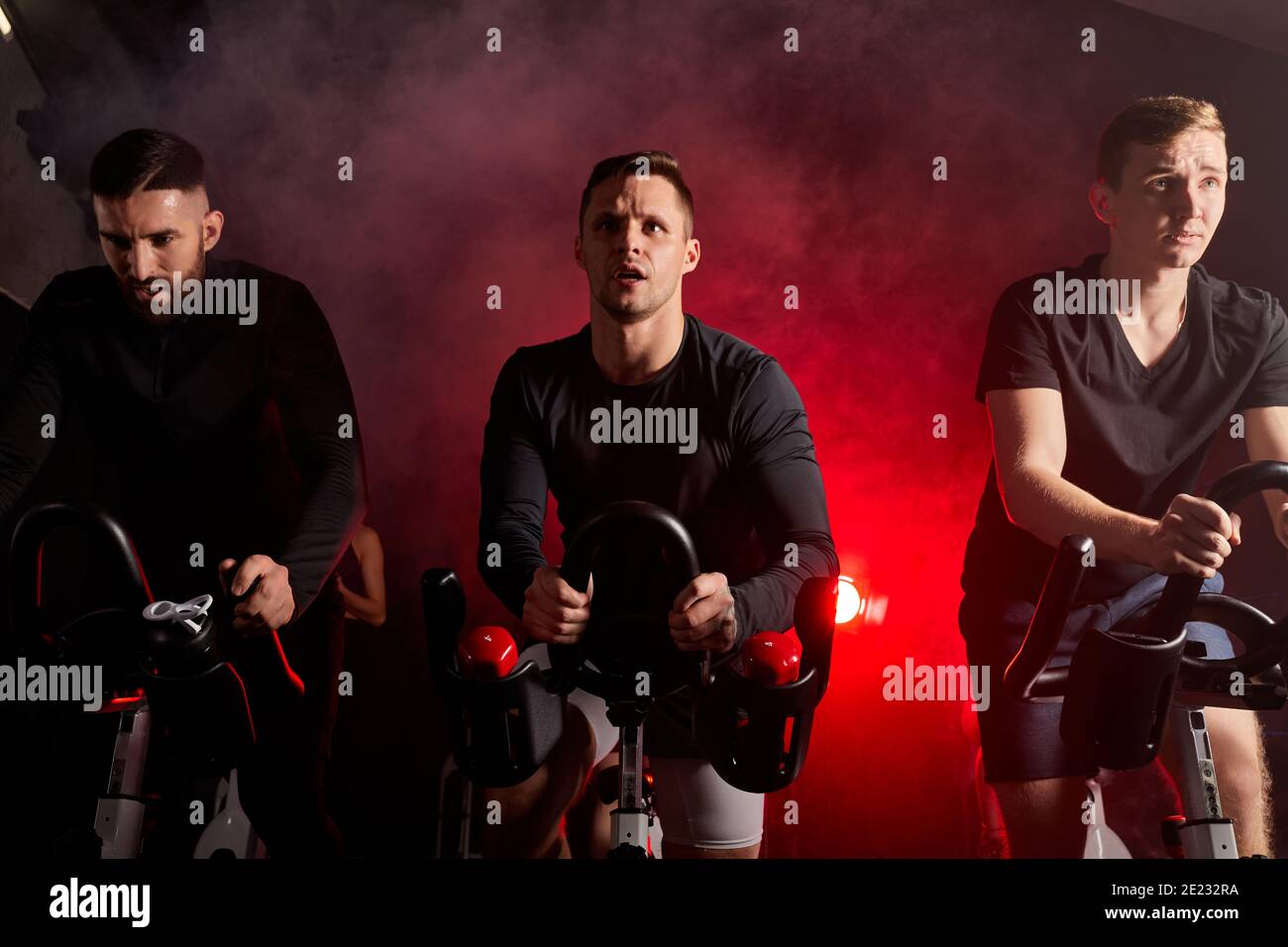 three men riding stationary bikes together during a cardio workout ...