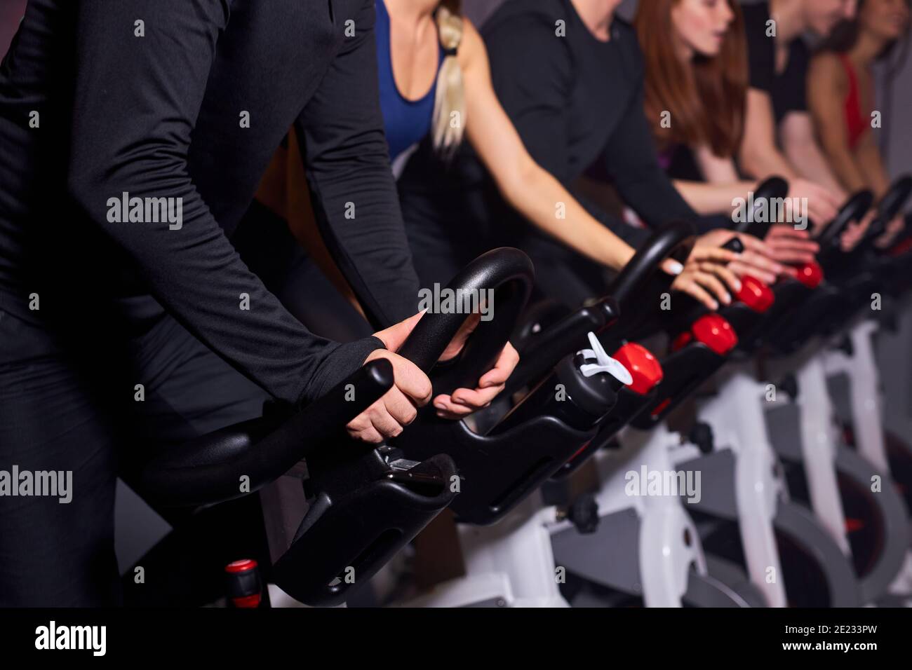 close-up hands of sporty people riding exercise bikes in gym, cropped ...