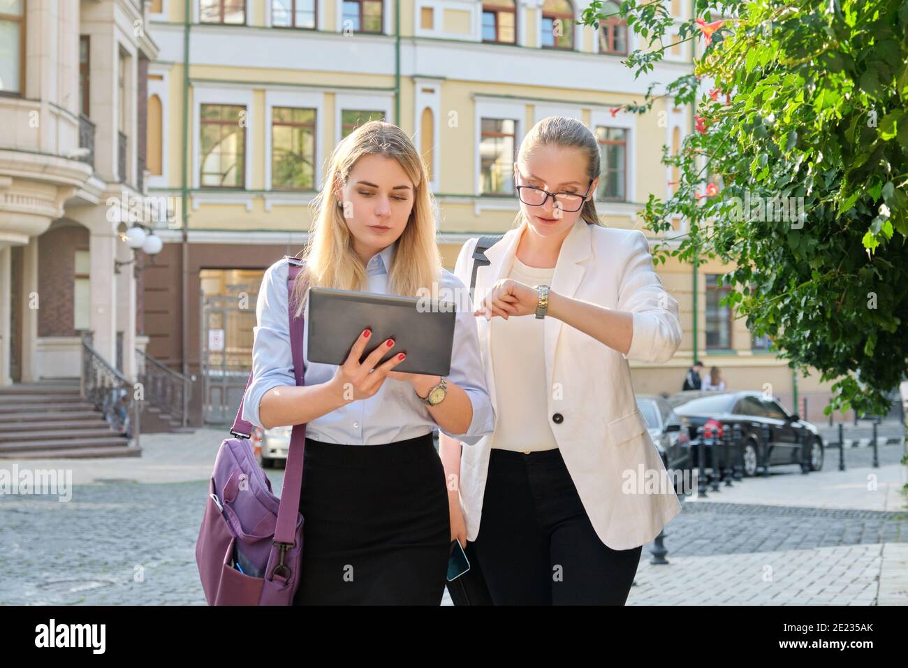 Two young businesswomen walking along city street, talking looking in ...