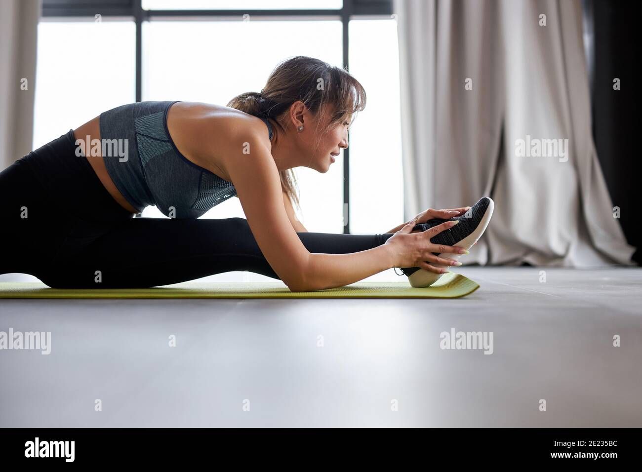 asian female is stretching on mat at home, training, stretch legs ...
