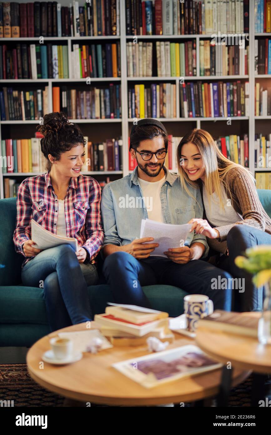 Group of three young students sitting in library and preparing exam ...
