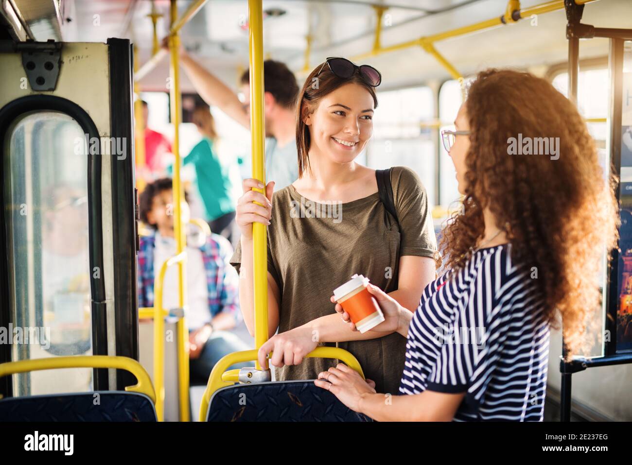 Two beautiful best friends are talking while standing in a bus full of ...