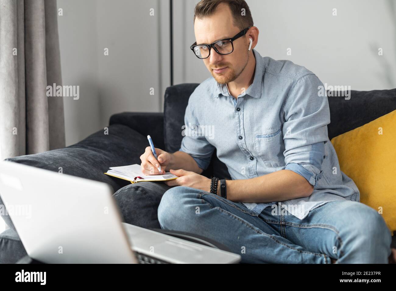 A young man with a laptop writing in a notebbook Stock Photo - Alamy