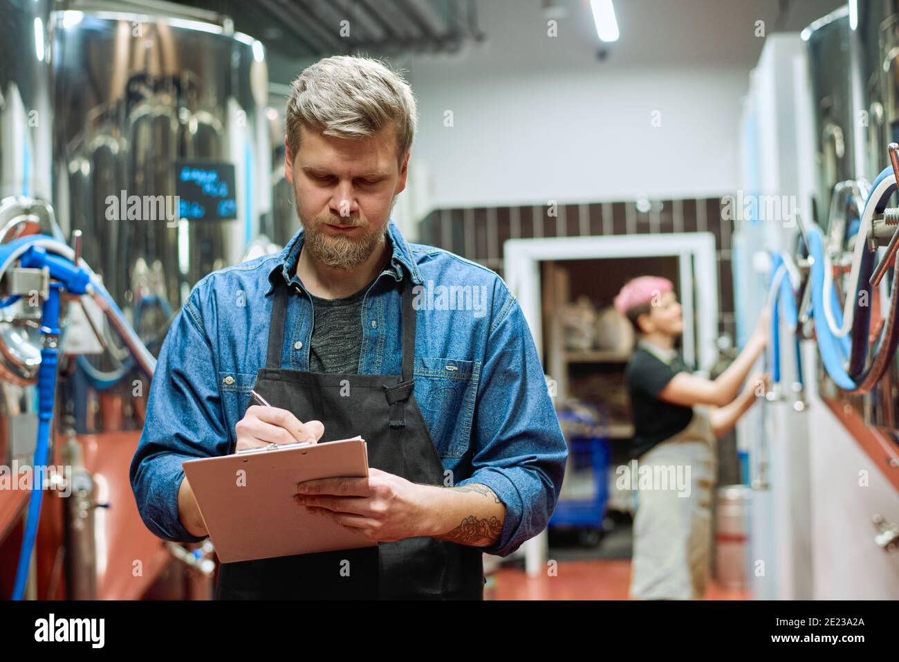 Young bearded male worker of beer production factory making notes while ...
