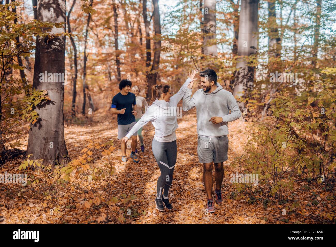 Runners giving high five while running. Forest in autumn exterior ...
