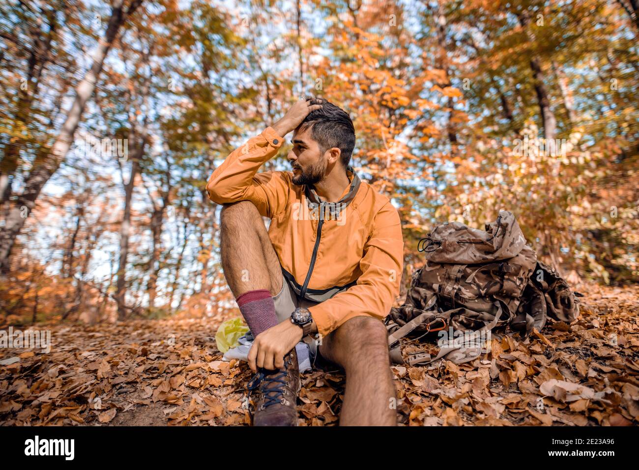 Hiker sitting on ground in woods in autumn. Next to him backpack ...