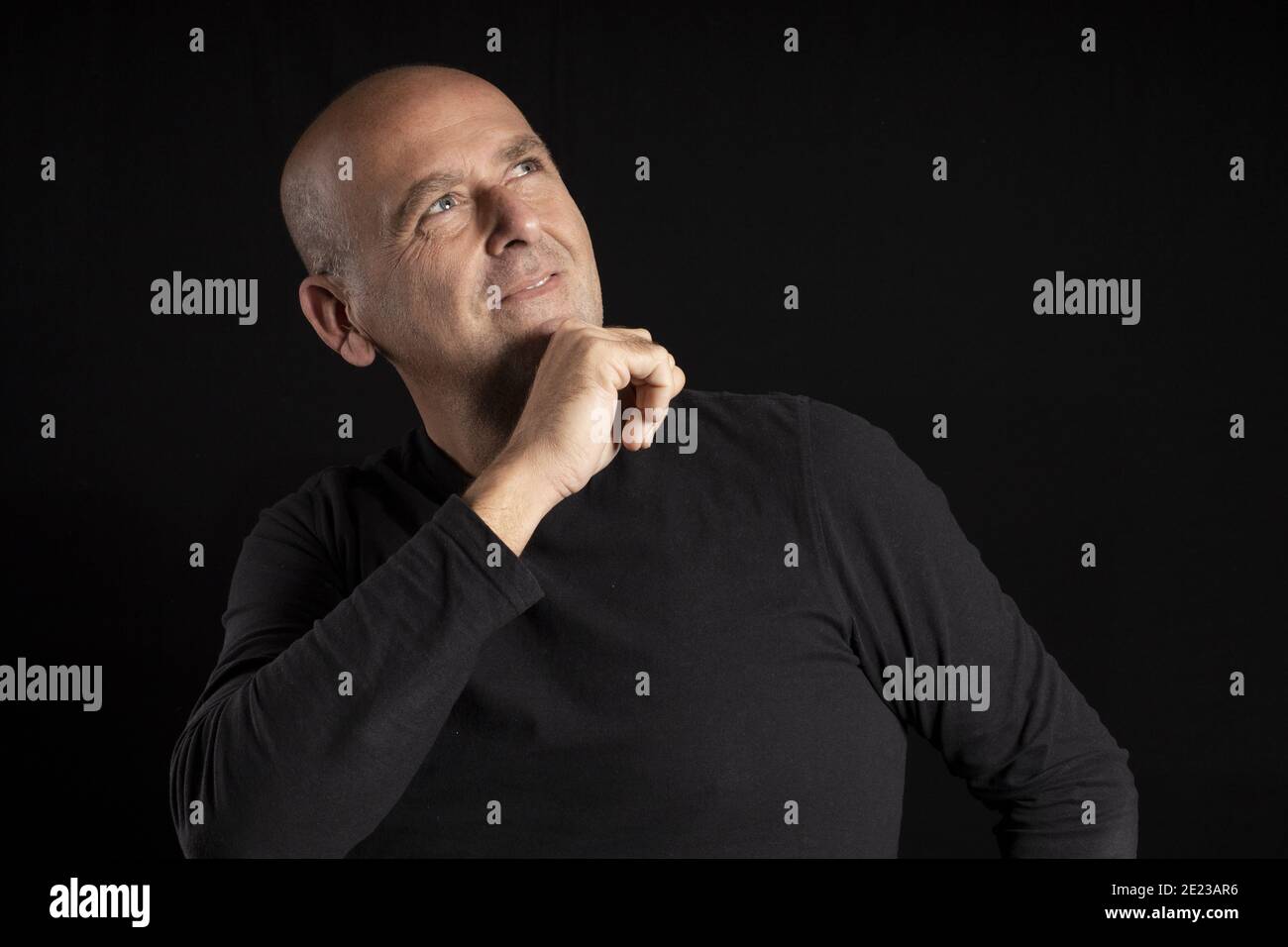 Middle-aged bald man with light eyes posing on black background looking ...