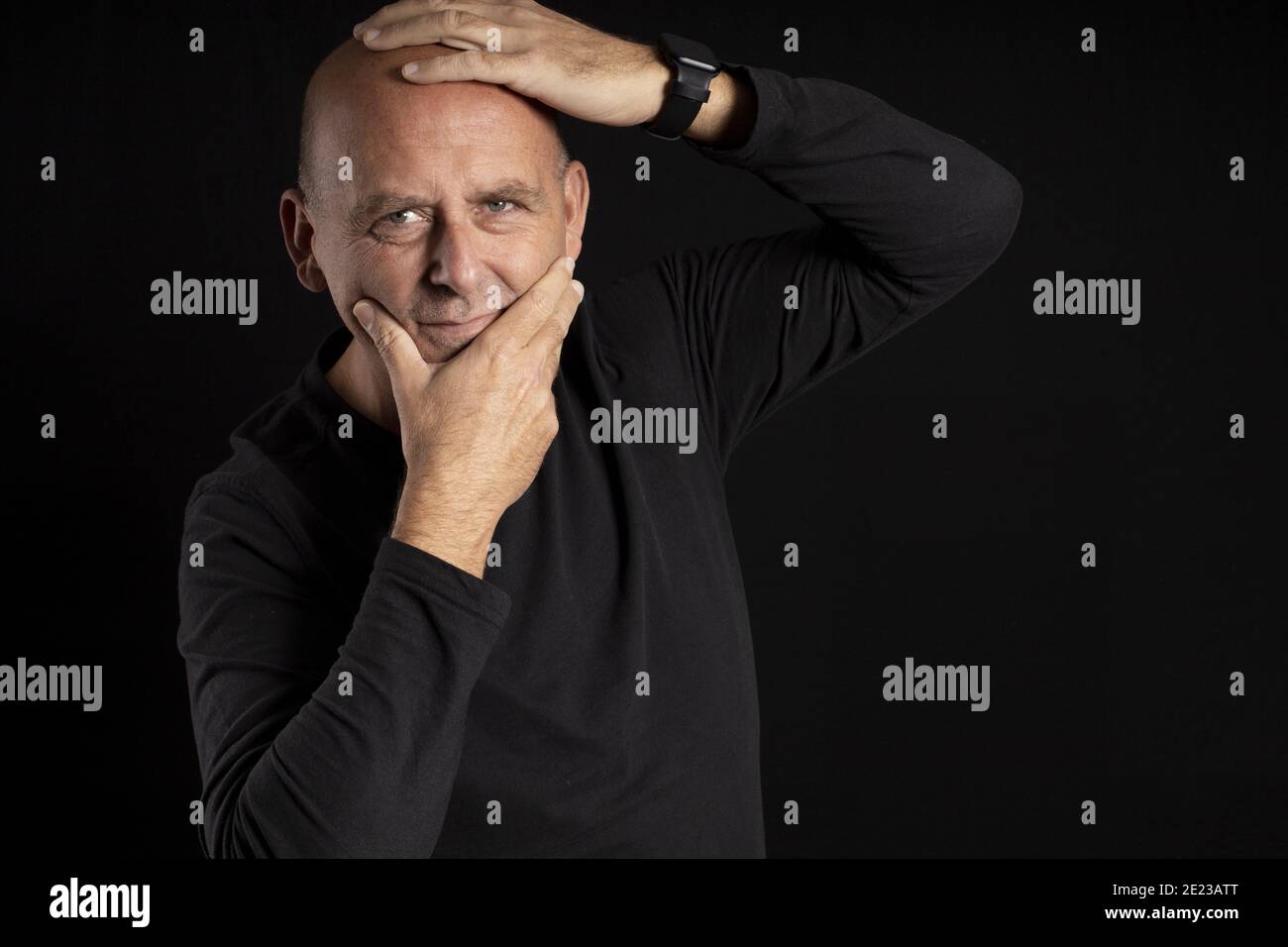 Portrait of a middle-aged bald man with light eyes posing on a black ...