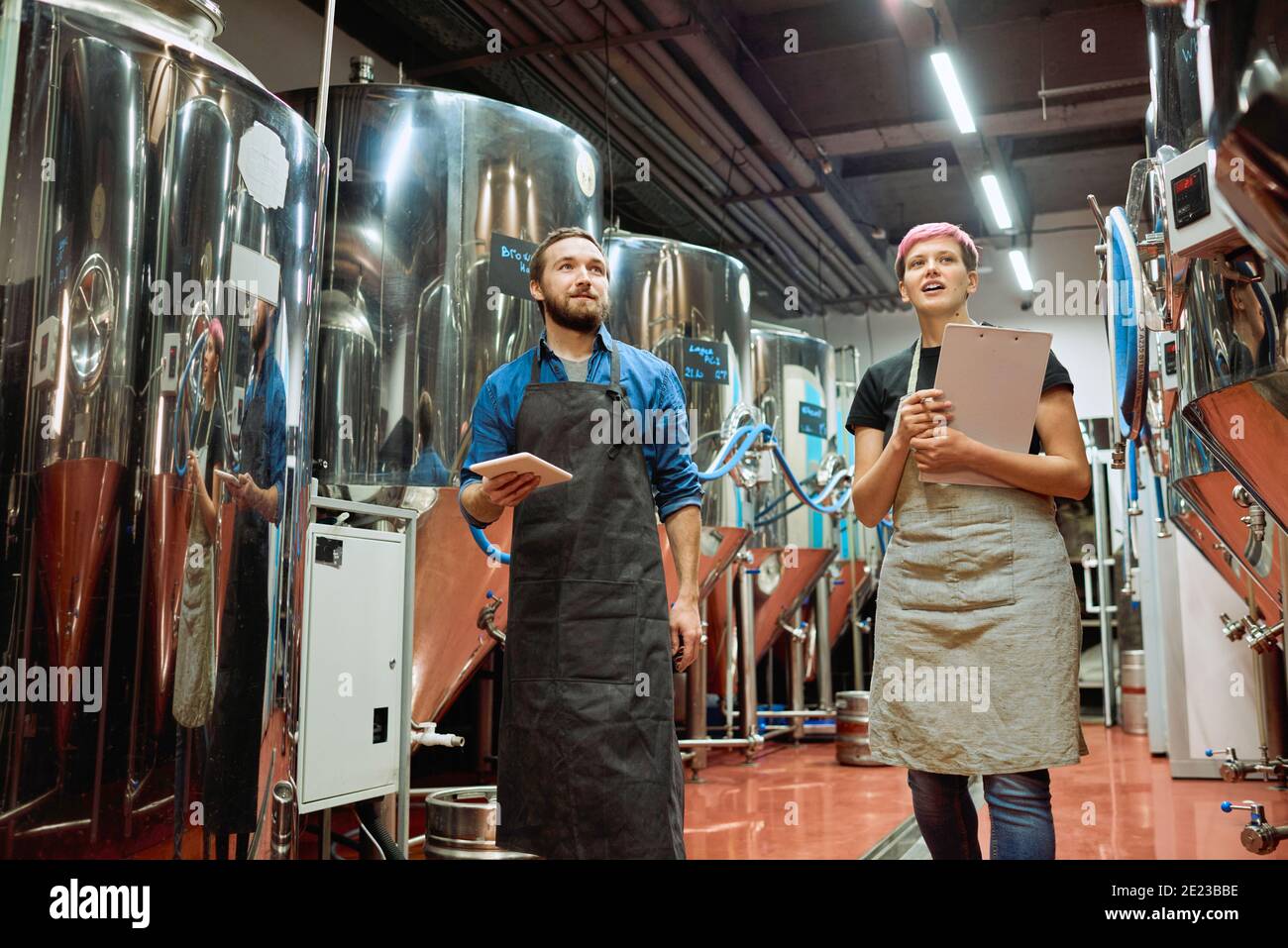 Two young workers of large contemporary beer production factory ...