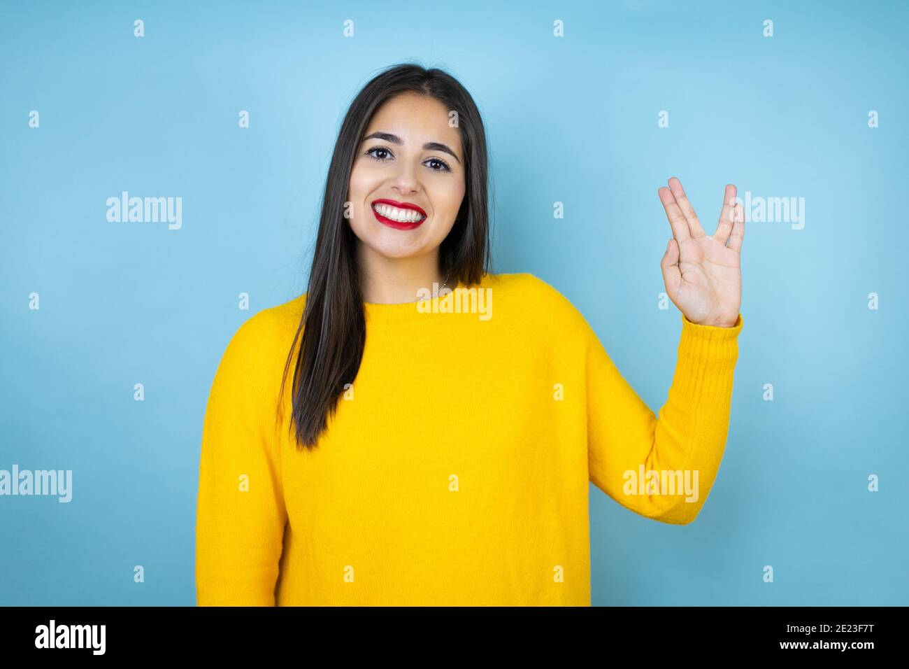Young beautiful woman wearing yellow sweater over isolated blue ...