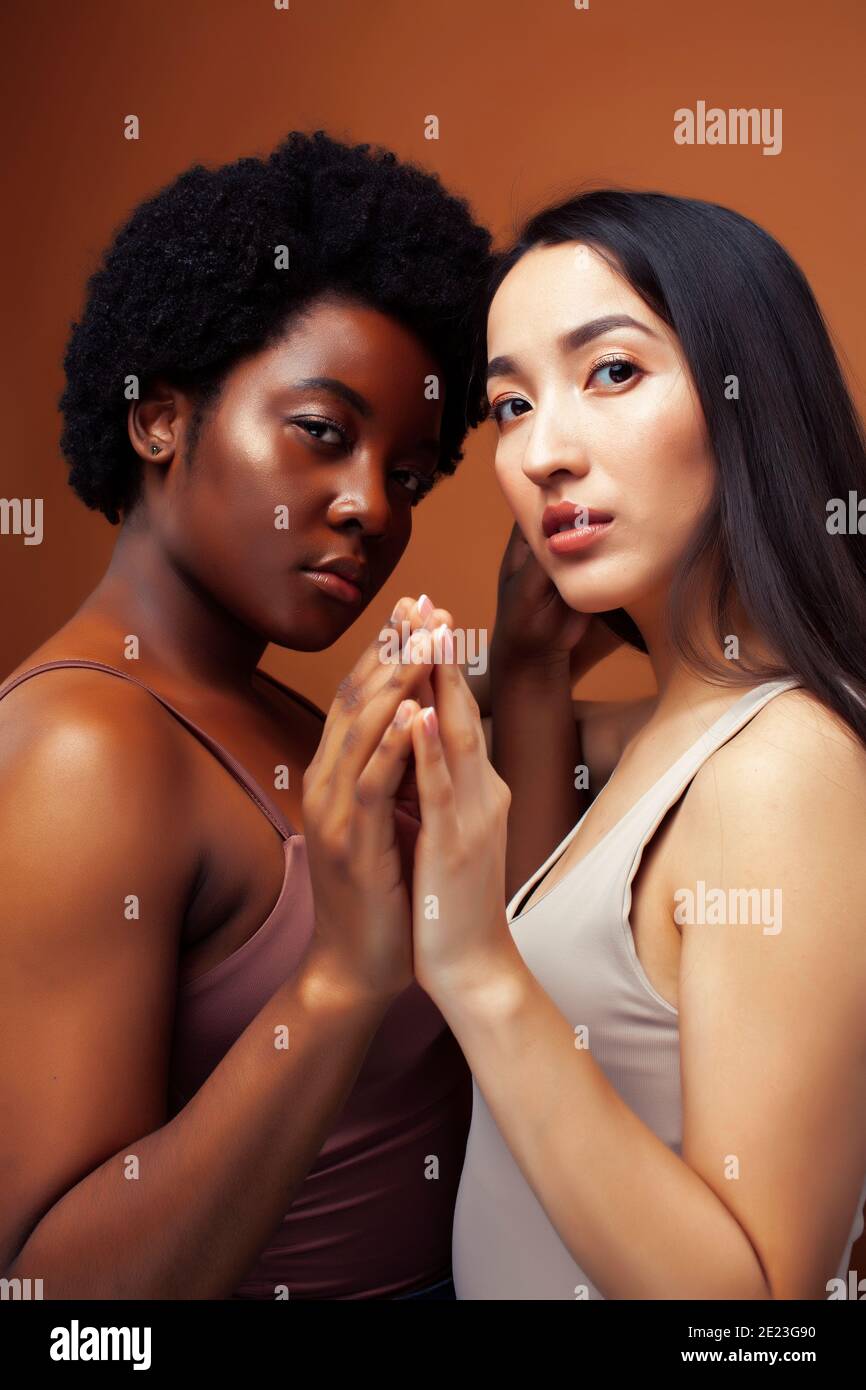 young pretty asian and afro woman posing cheerful together on brown ...