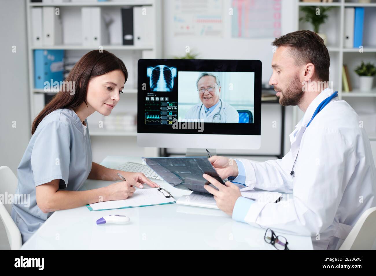 Two practitioners sitting in front of computer monitor and discussing x ...