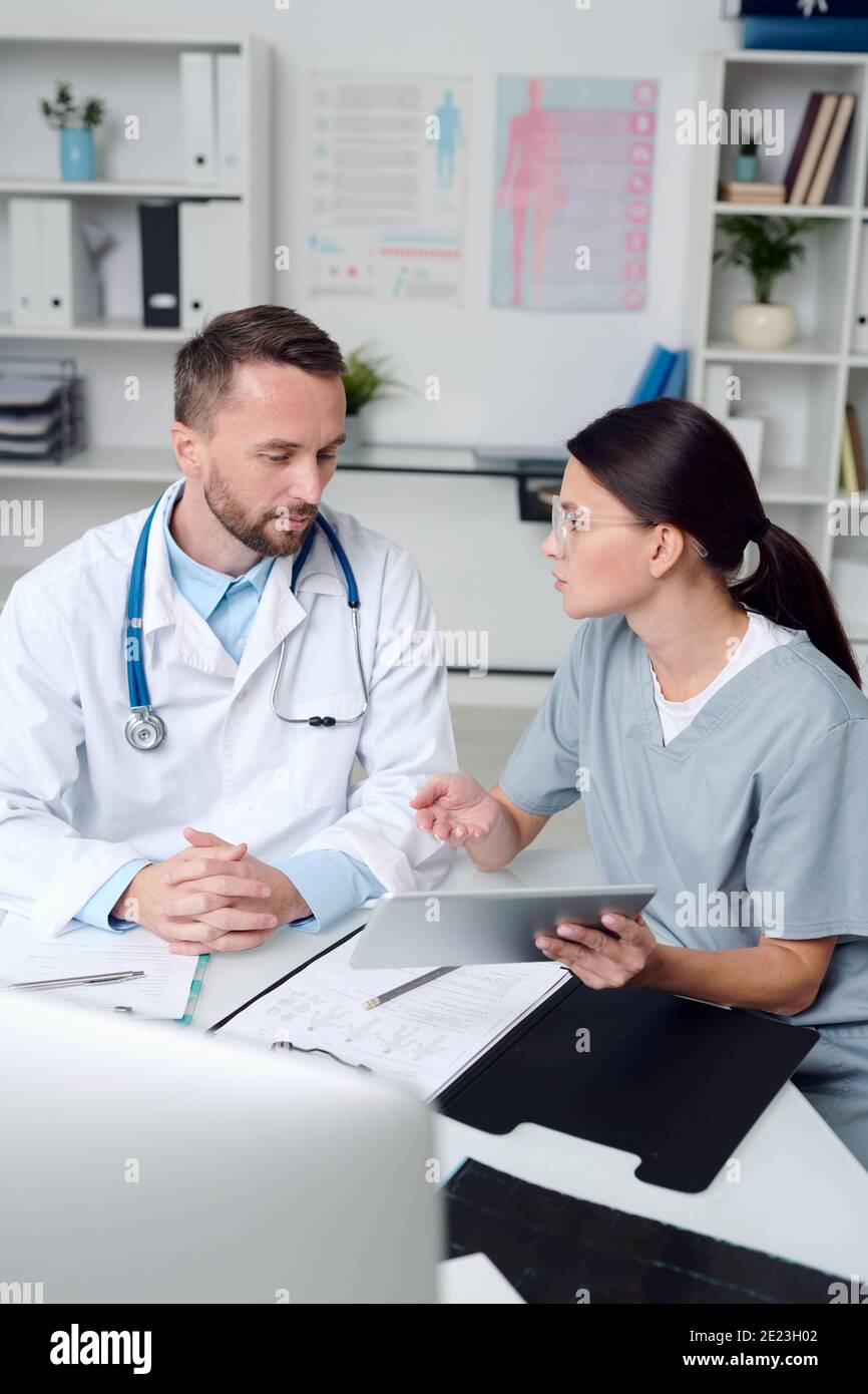 Two young confident clinicians in uniform sitting by desk in front of ...