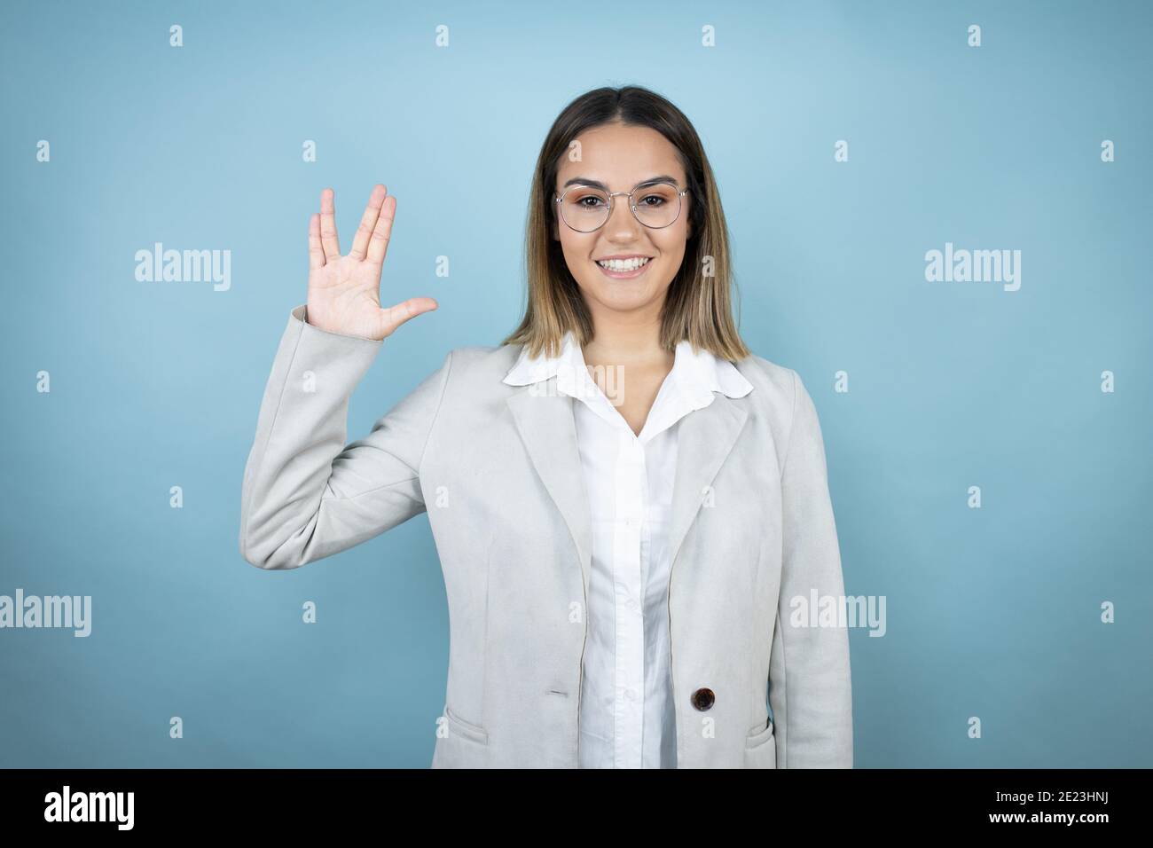 Young business woman over isolated blue background doing star trek ...