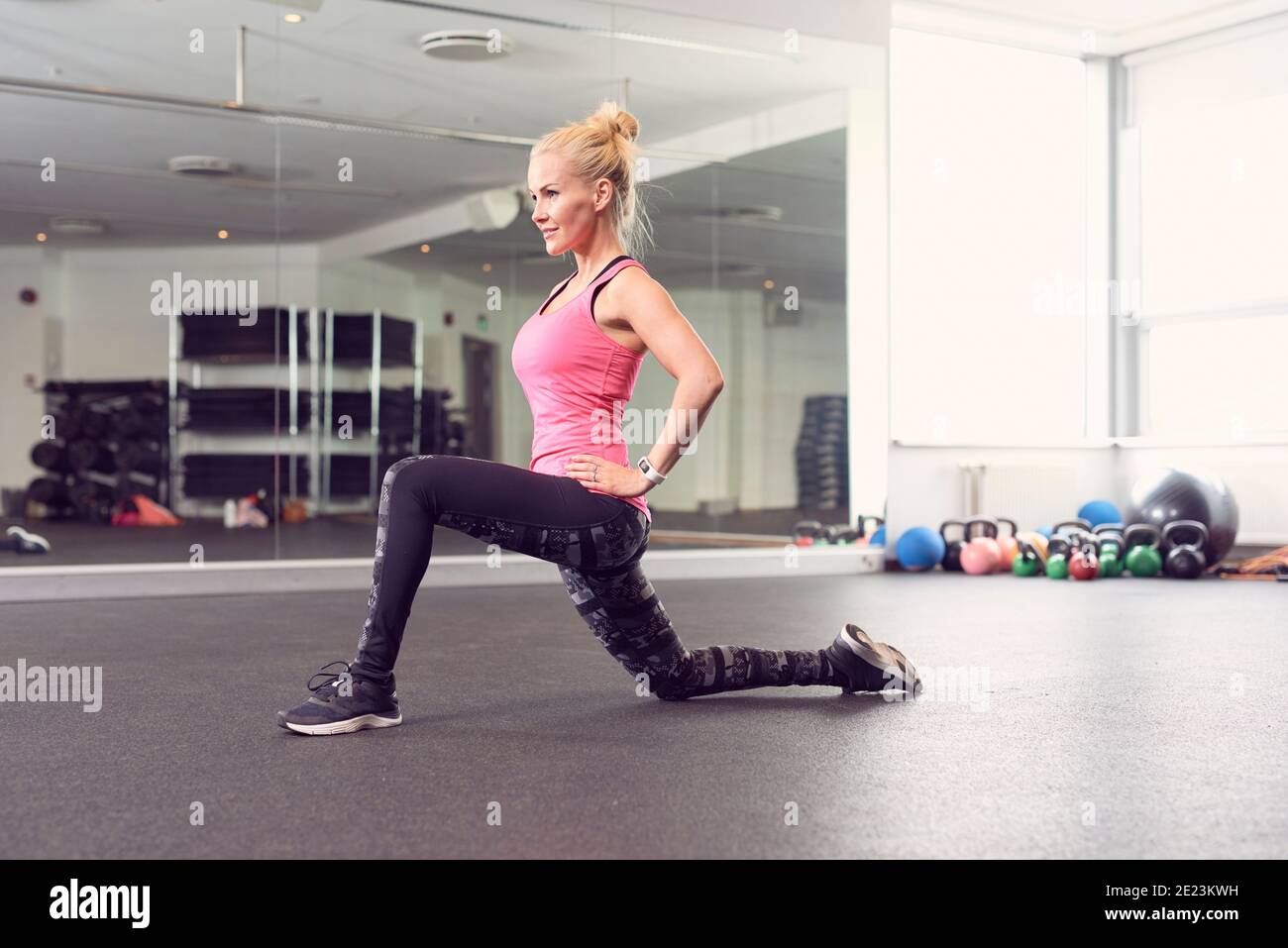 Positive young fit female doing lunges during fitness workout in modern ...