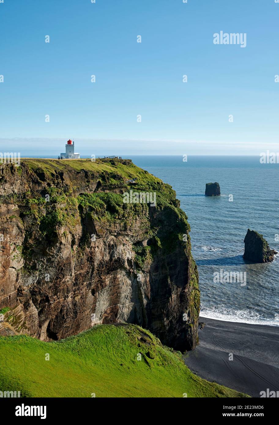 Small lonely lighthouse on edge of green cliff above calm rippling ...
