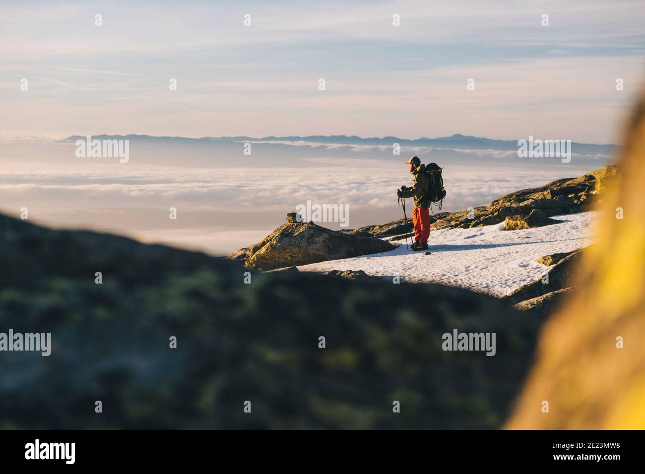 Young man wearing cap and looking at sun rising above horizon, against ...
