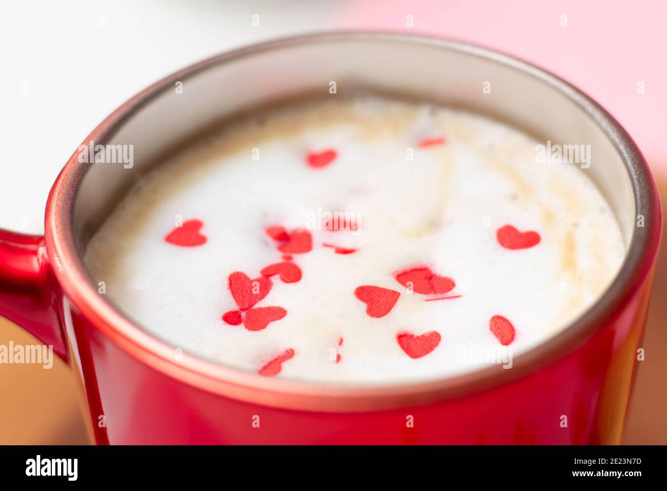 Red latte cup with sprinkles in the form of red hearts on foam on pink ...