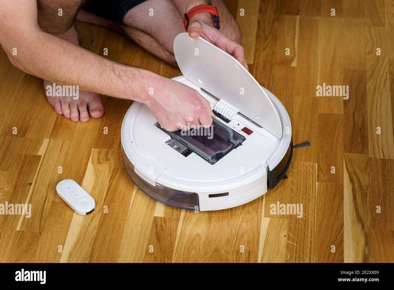 Caucasian young man doing white robot vacuum cleaner maintenance ...