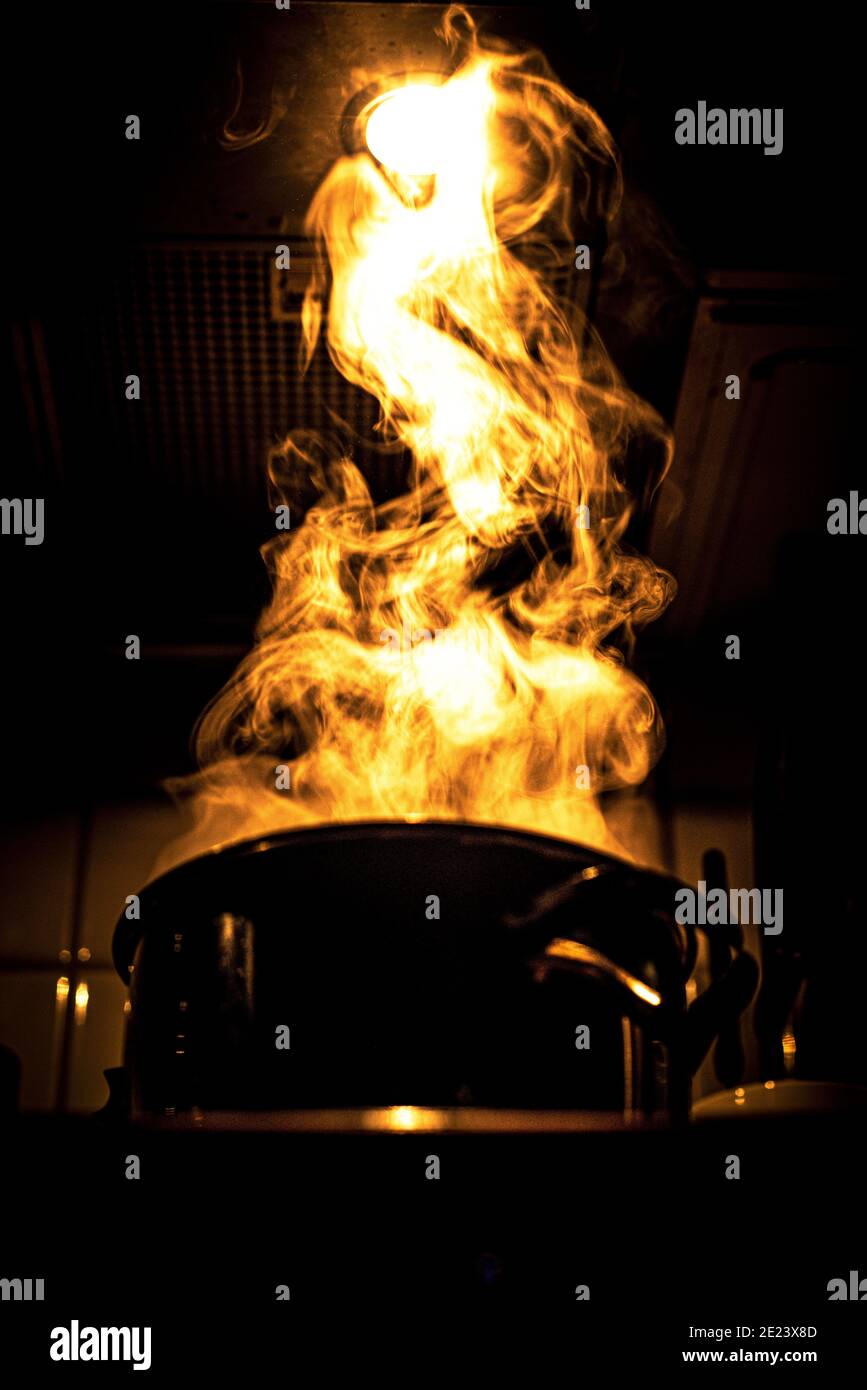 Vertical shot of a saucepan on fire with huge firery flames shooting up ...